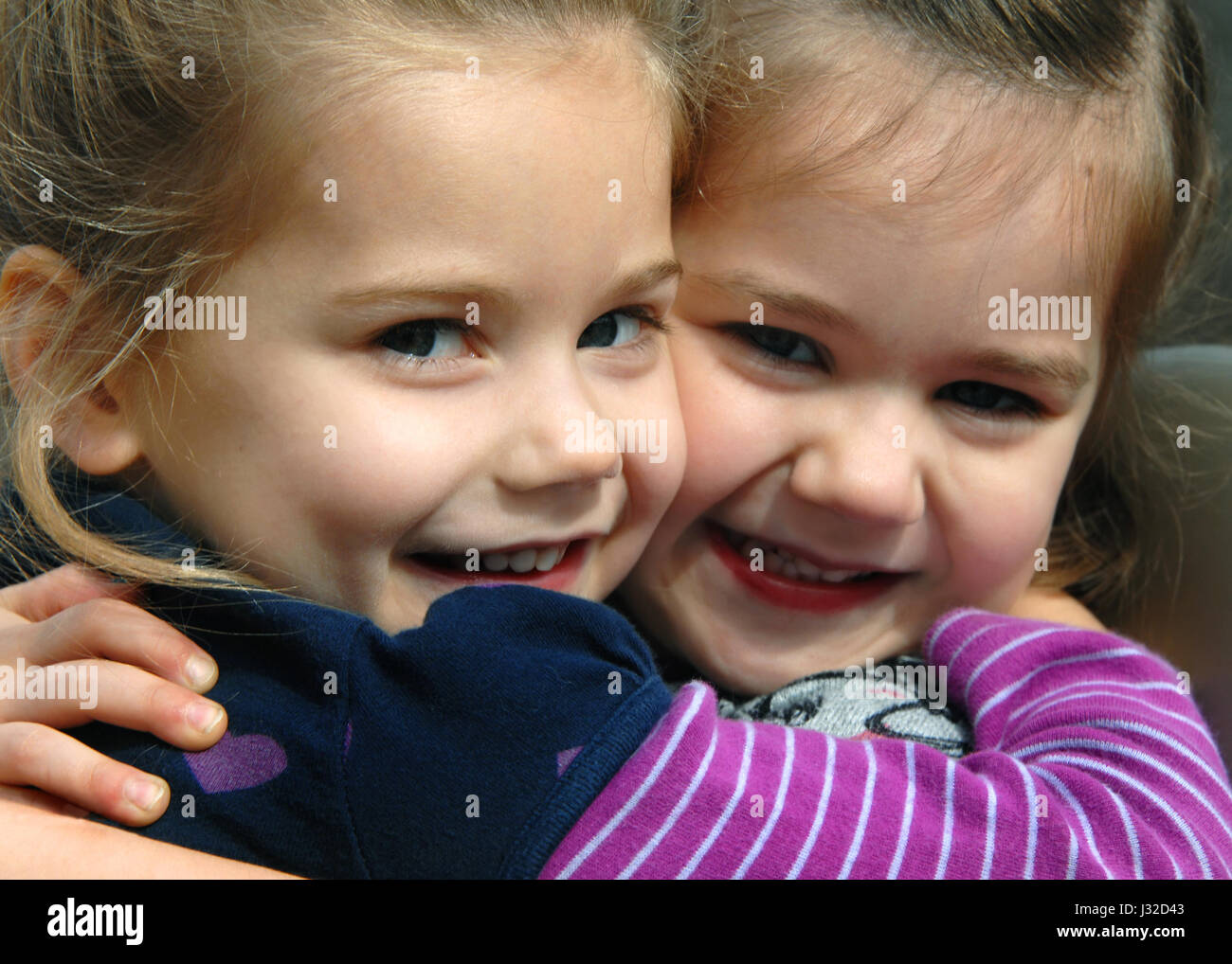 Two sisters hug and squeeze each other. Both are beaming and smiling at ...