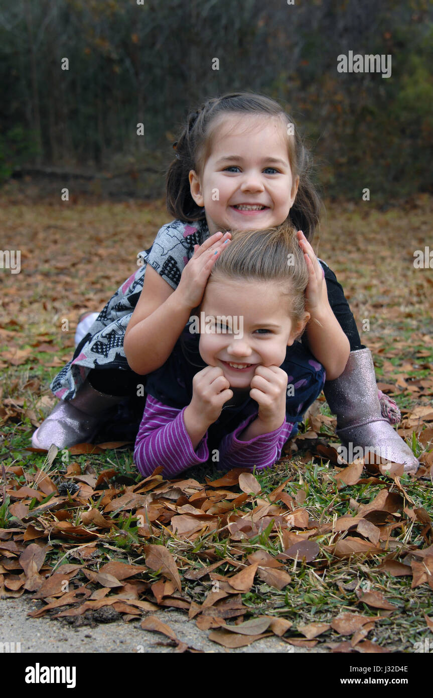 Two sisters tumble in the grass and leaves on a Fall morning. One ...