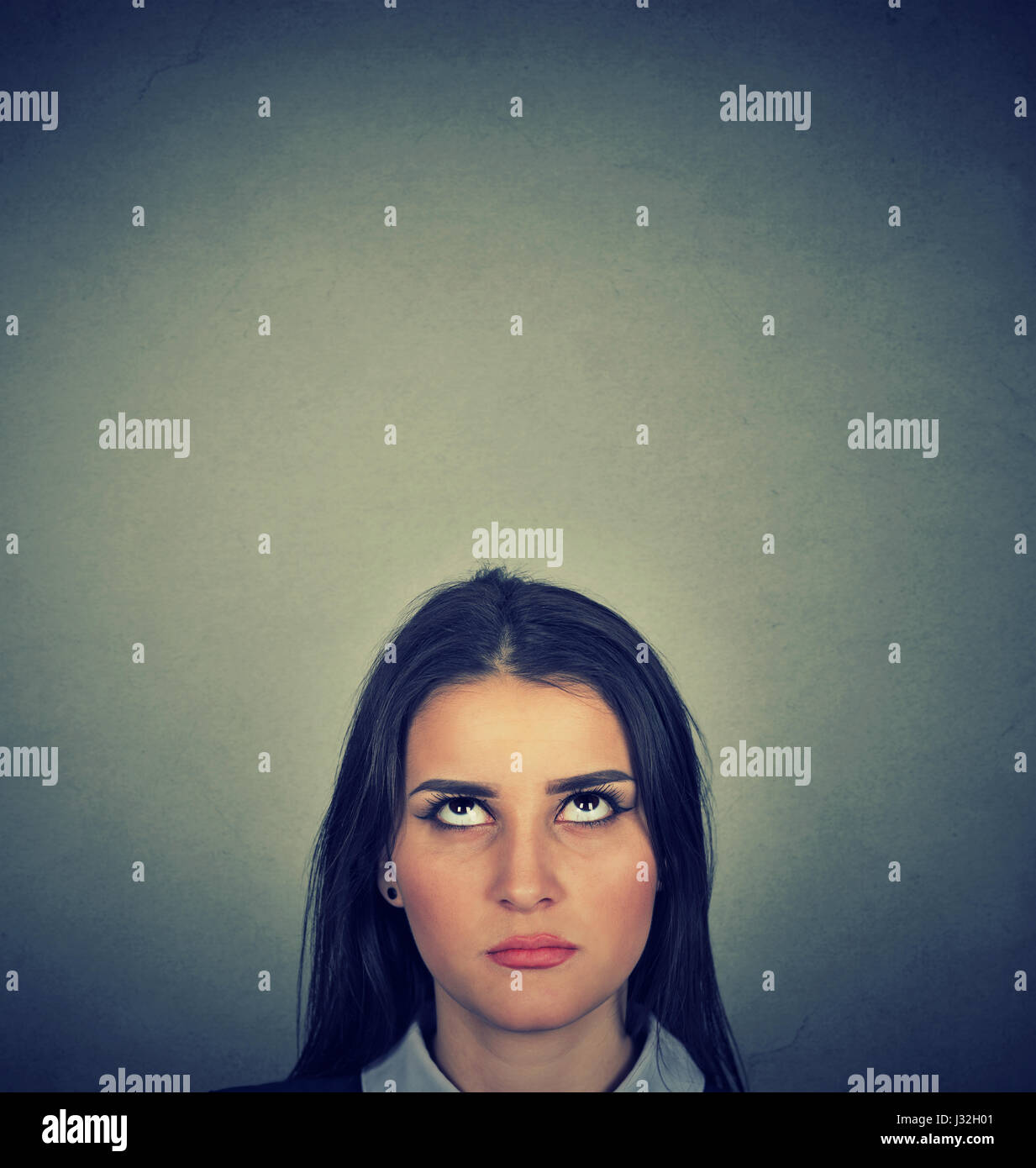 Young skeptical woman looking up isolated on gray wall background with ...