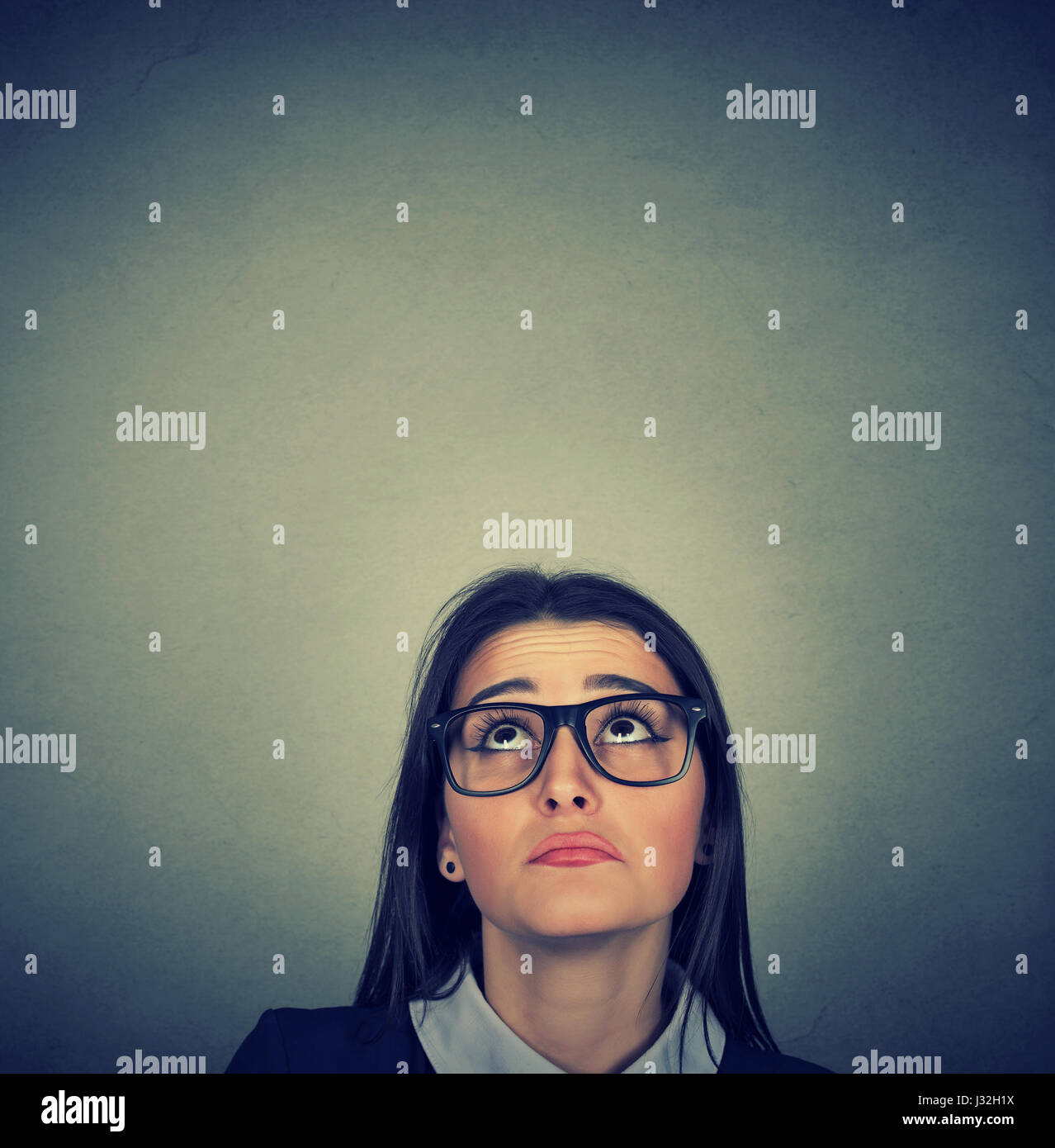 Young skeptical woman looking up isolated on gray wall background with ...
