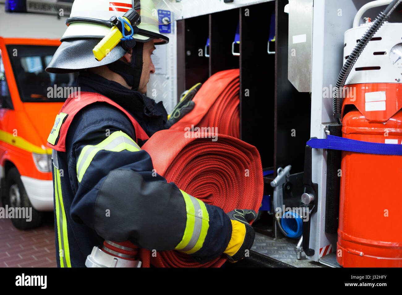 German firefighter in the fire station with a water hose in the hand ...