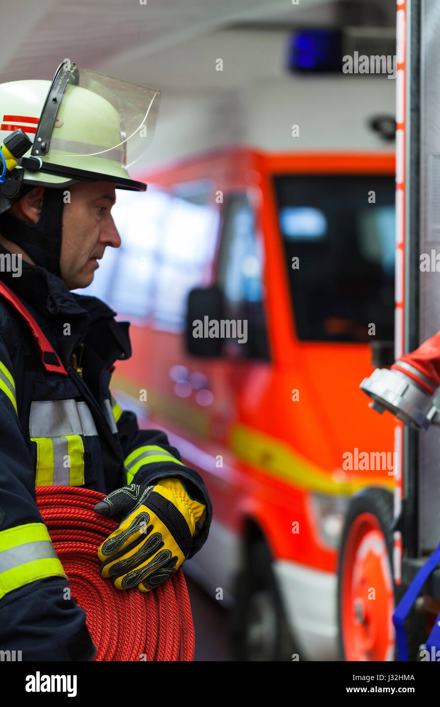 German firefighter in the fire station with a water hose in the hand ...