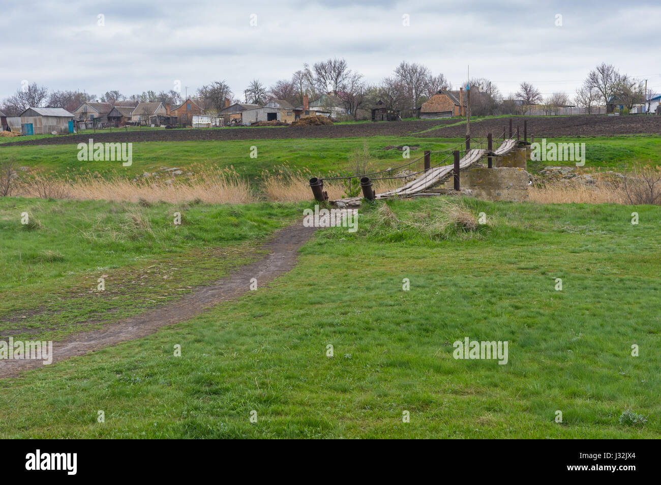 Spring landscape with meadow and old foot-bridge over small river ...