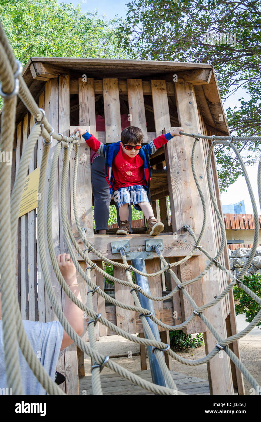 A young boy crosses a rope bridge which is part of a climbing frame in ...
