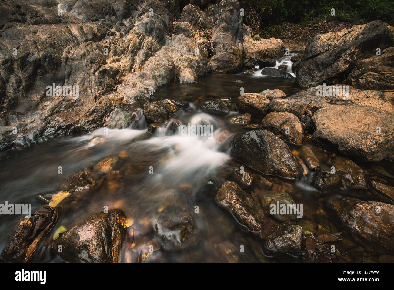 Dark tone of brown rock river with flowing cold water through the rocks ...