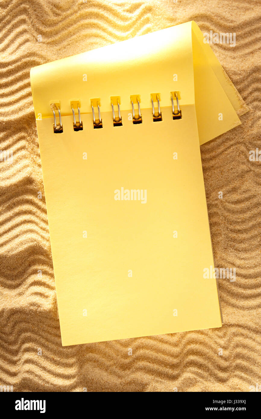 Open yellow notepad on sand background in light Stock Photo - Alamy