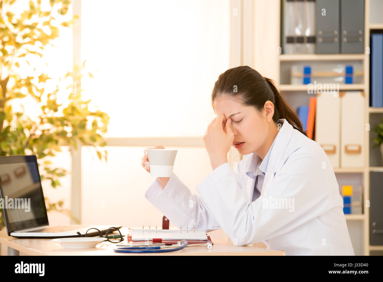Tired and depressed doctor in medical office drinking coffee touch ...