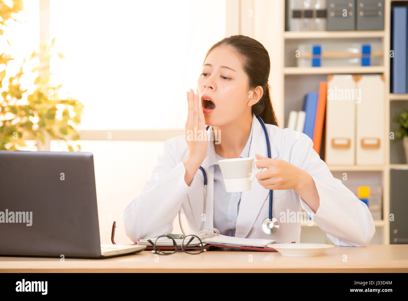 sleepy and tired doctor with coffee working in clinic office. mixed ...