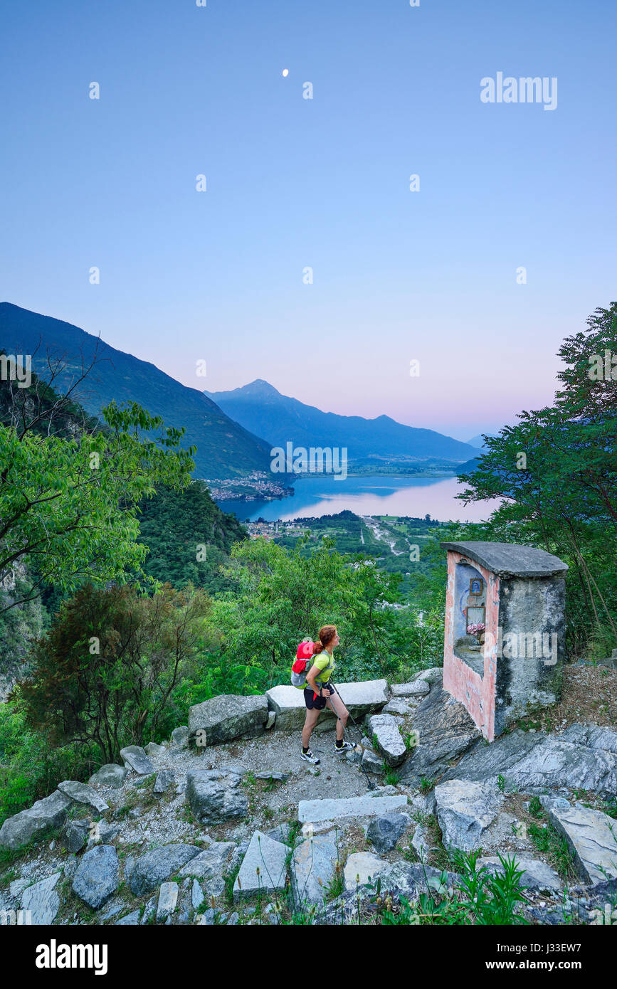 Woman hiking standing in front of chapel, Lago di Mezzola in background ...