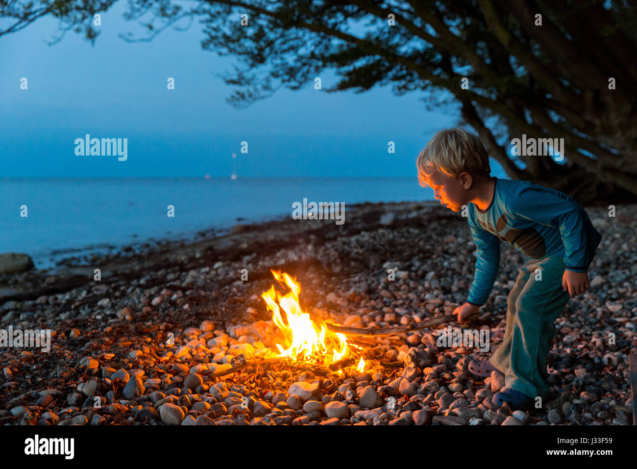 Boy at a campfire at Baltic Sea beach, Naesgaard, Falster, Denmark ...