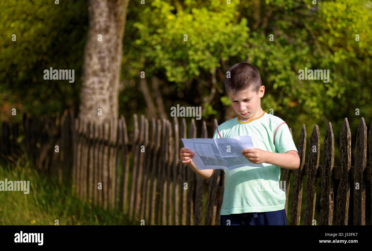 Boy looking in map next to the village fence Stock Photo - Alamy
