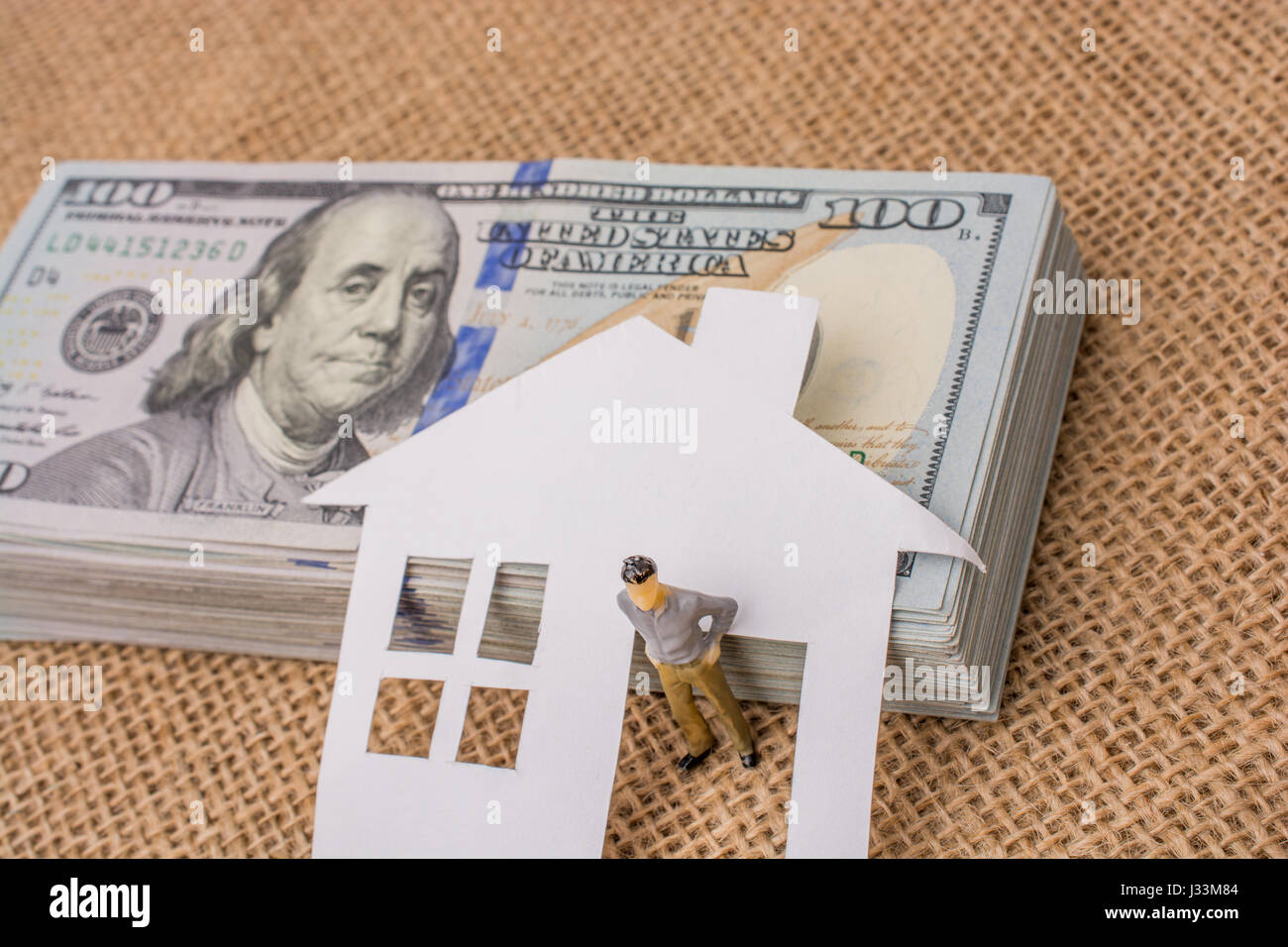 Paper house and a man figurine beside a bundle of US dollar banknote ...