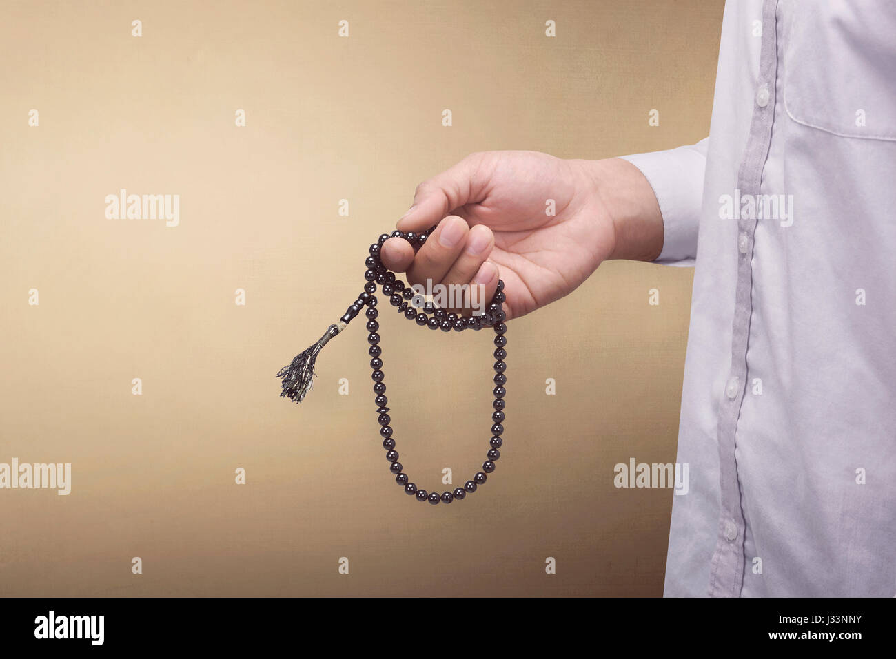 Hand of muslim man praying while holding tasbih over brown background ...