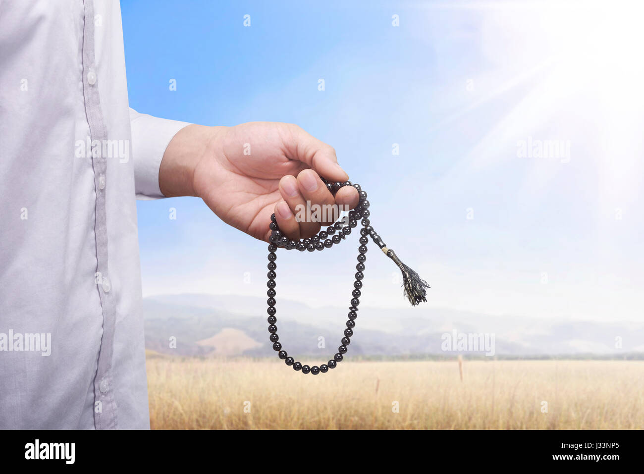 Hand of muslim man praying while holding tasbih with meadow field ...