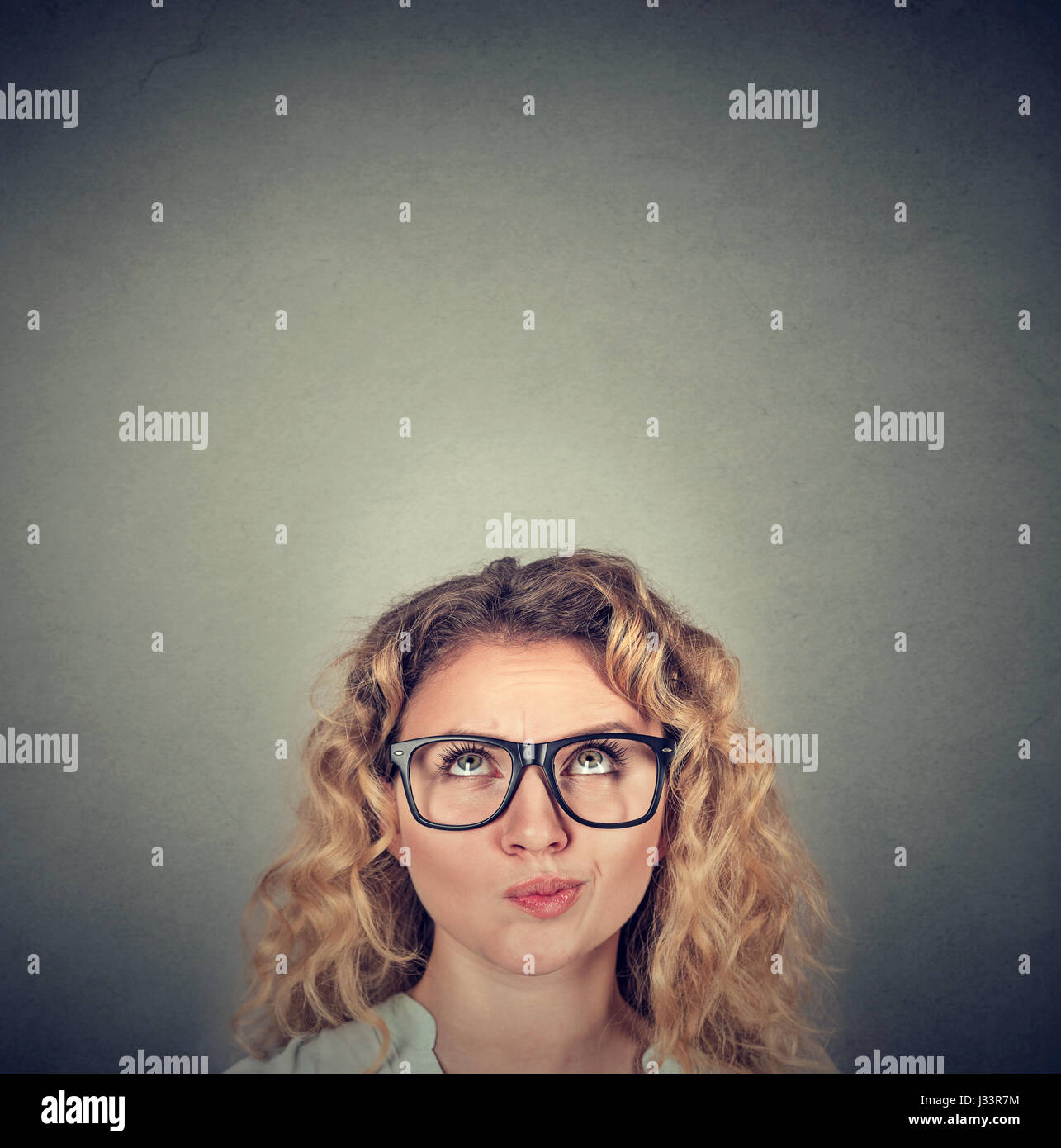 Young skeptical woman looking up isolated on gray wall background with ...