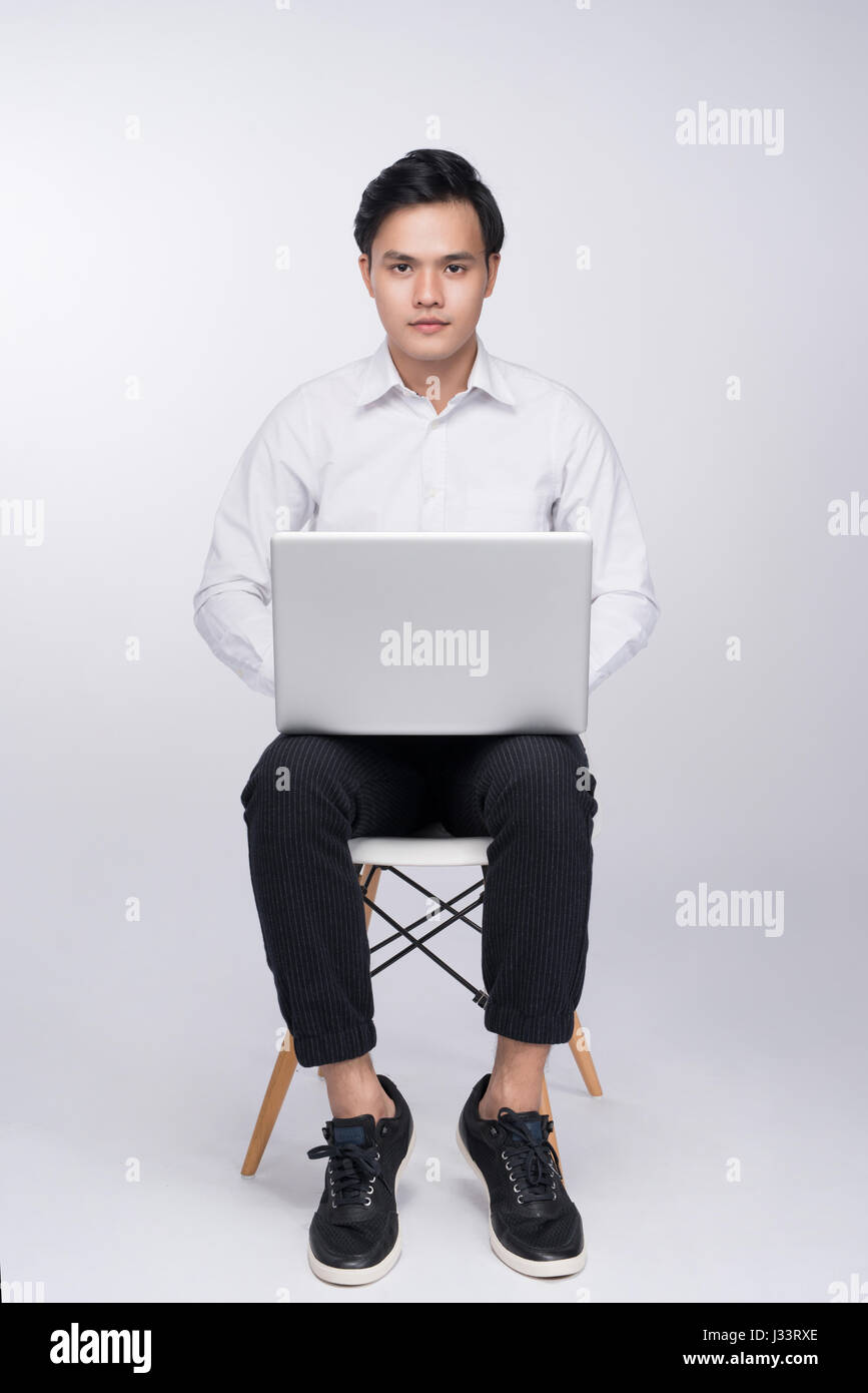 Smart casual asian man seated on chair, using laptop in studio ...