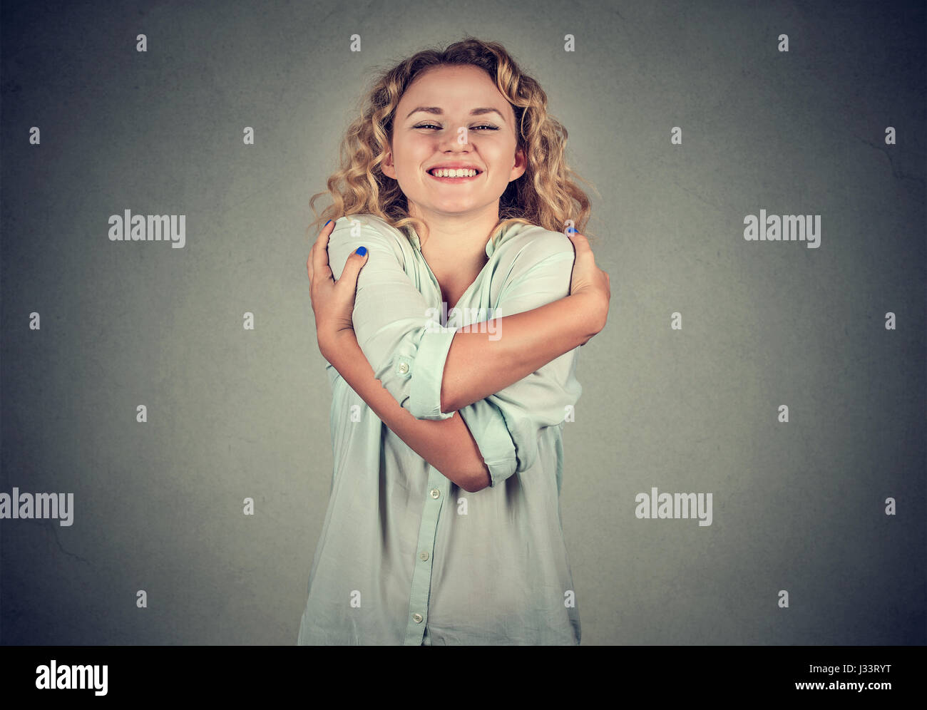Smiling woman holding hugging herself isolated gray wall background ...