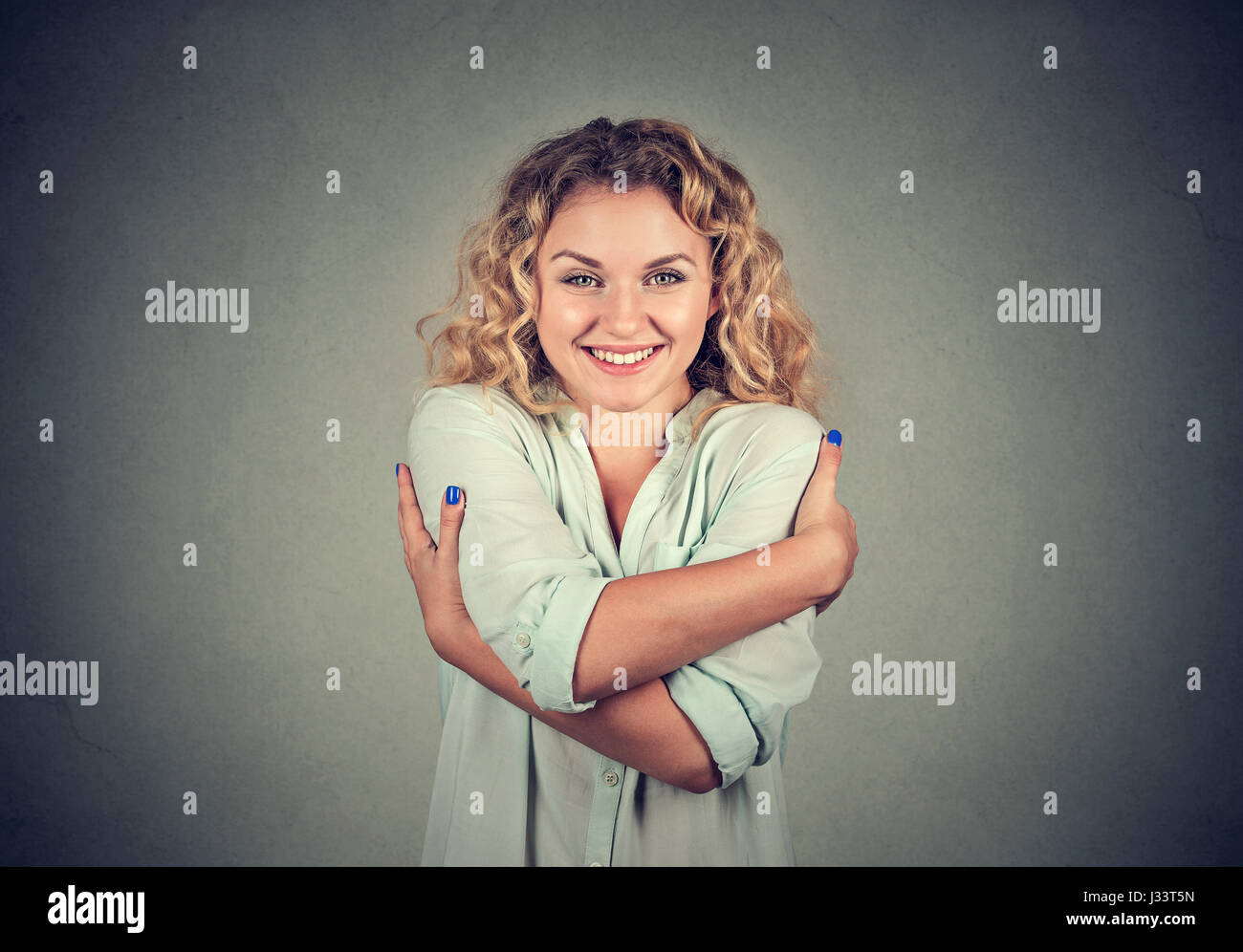 Smiling woman holding hugging herself isolated gray wall background ...
