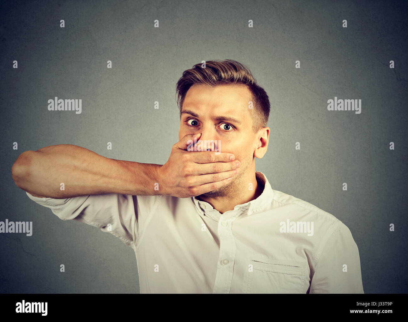 Scared young man covering mouth with hand isolated on gray wall ...