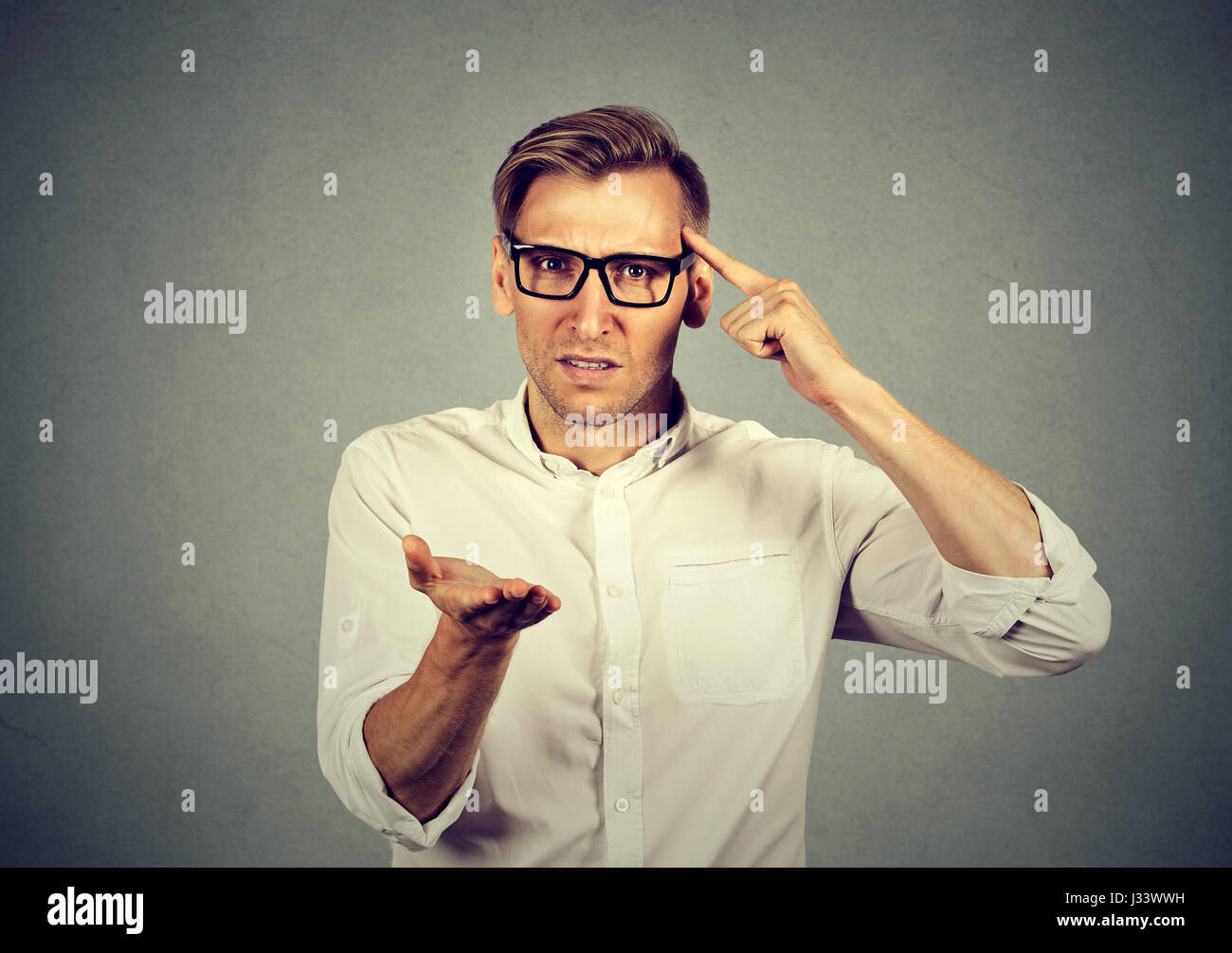 Angry mad young man gesturing with finger against temple asking are you ...