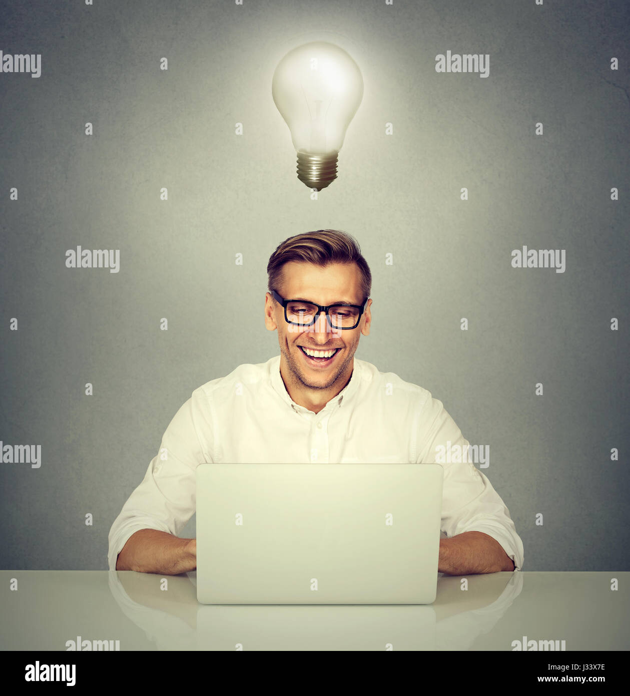 Smiling young man in front of a computer with light bulb over his head ...