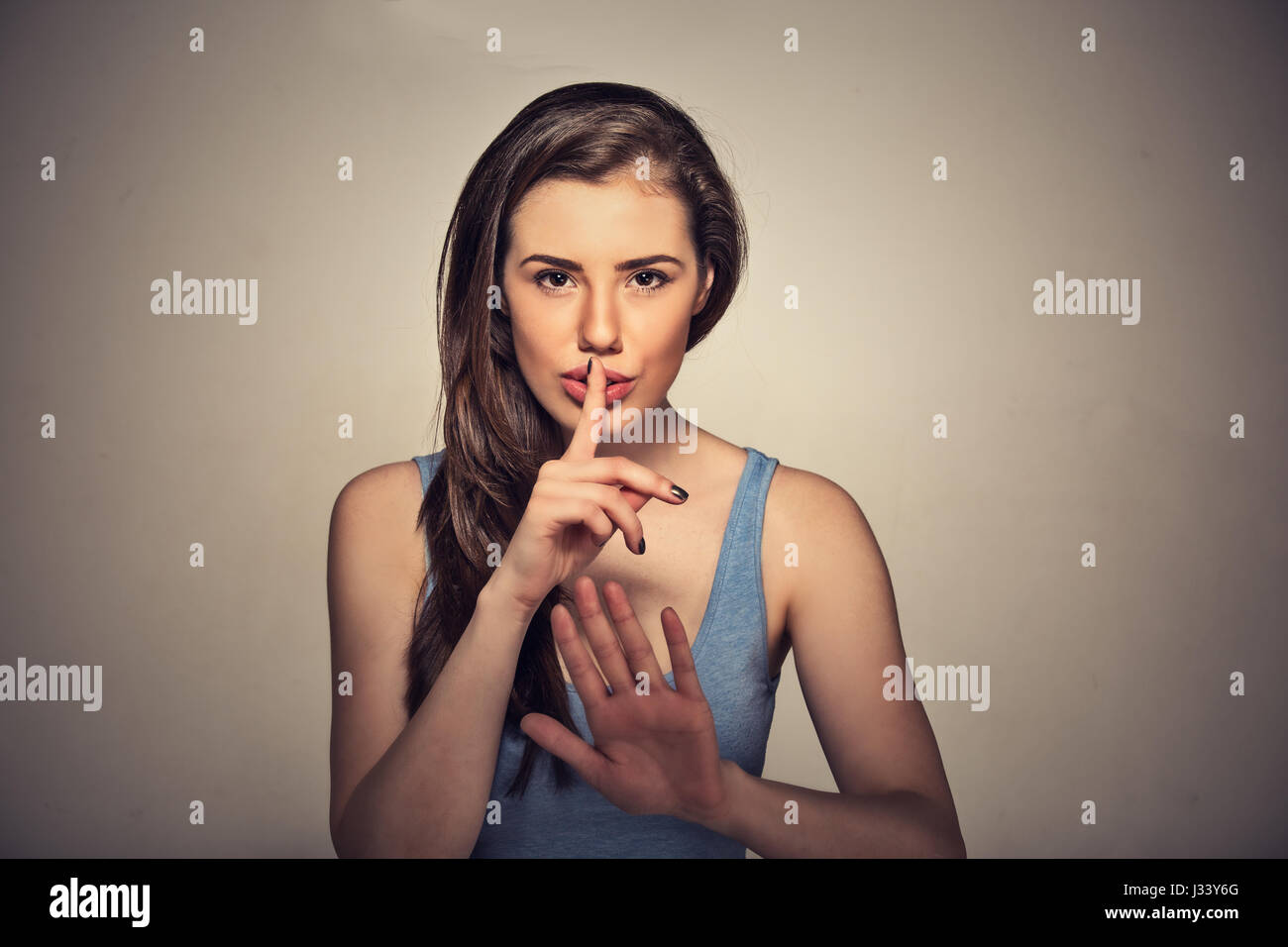 Portrait of young beautiful woman with finger on lips isolated on gray ...
