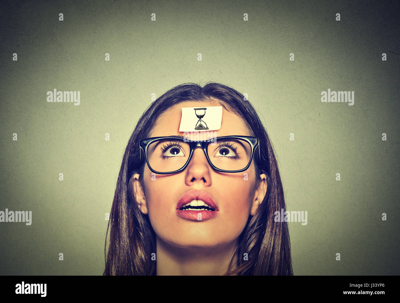 Thinking young woman with sand clock sign sticker on her forehead ...