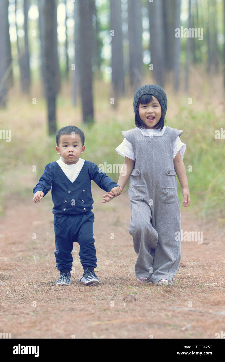 asian little cute brother of boy and girl hand in hand walking in pine ...