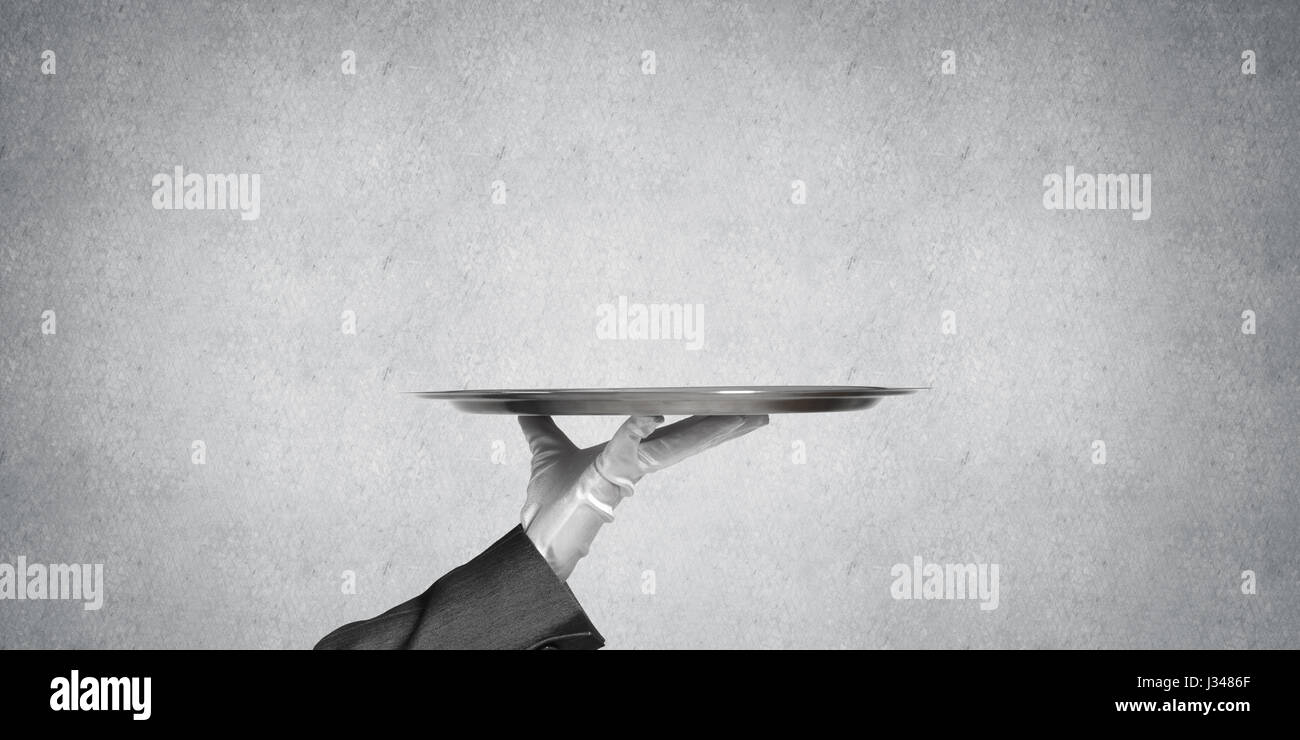 Hand of butler holding empty metal tray against concrete background ...