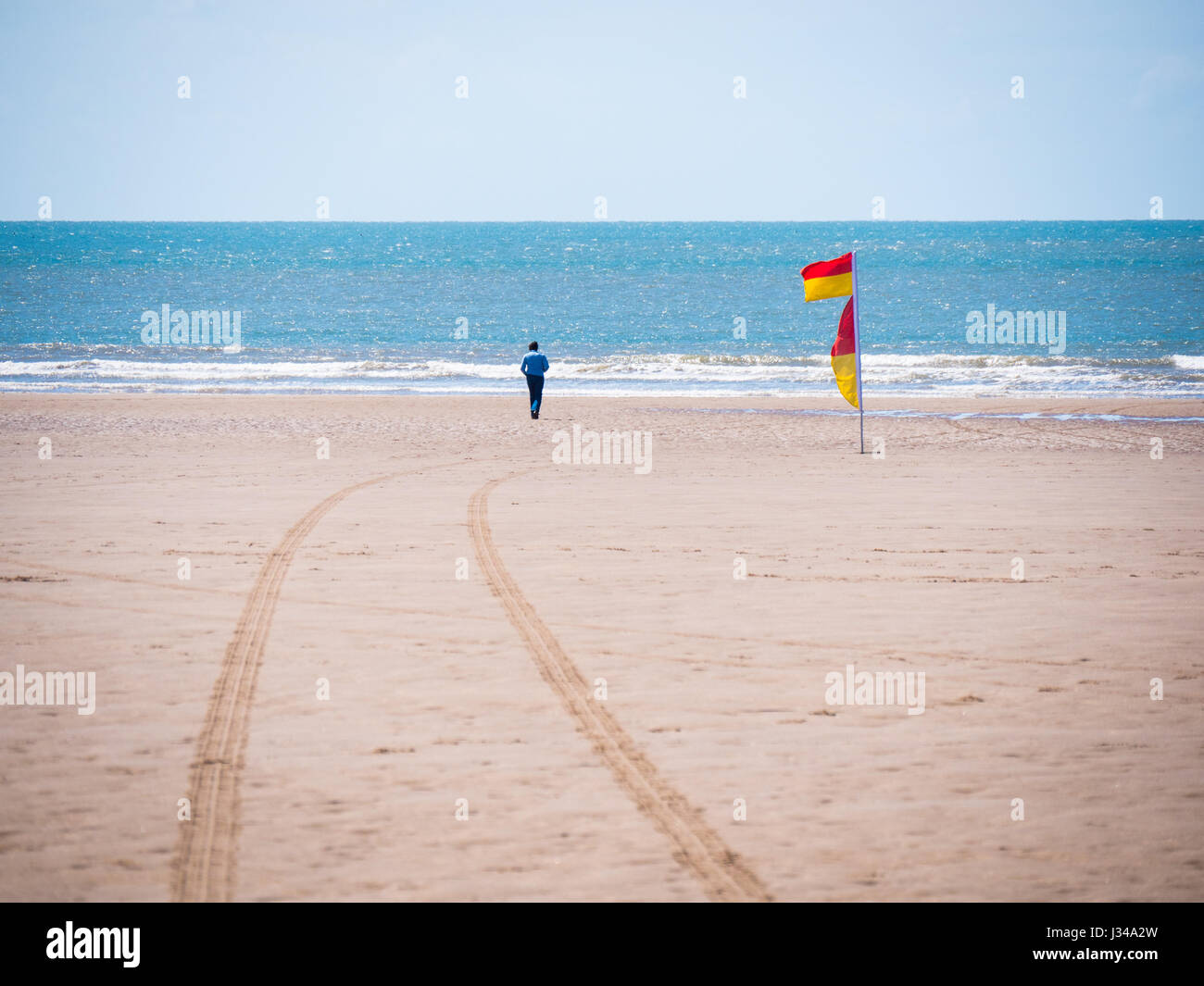 Man walking towards beach flags and the surf at Croyde beach on a ...