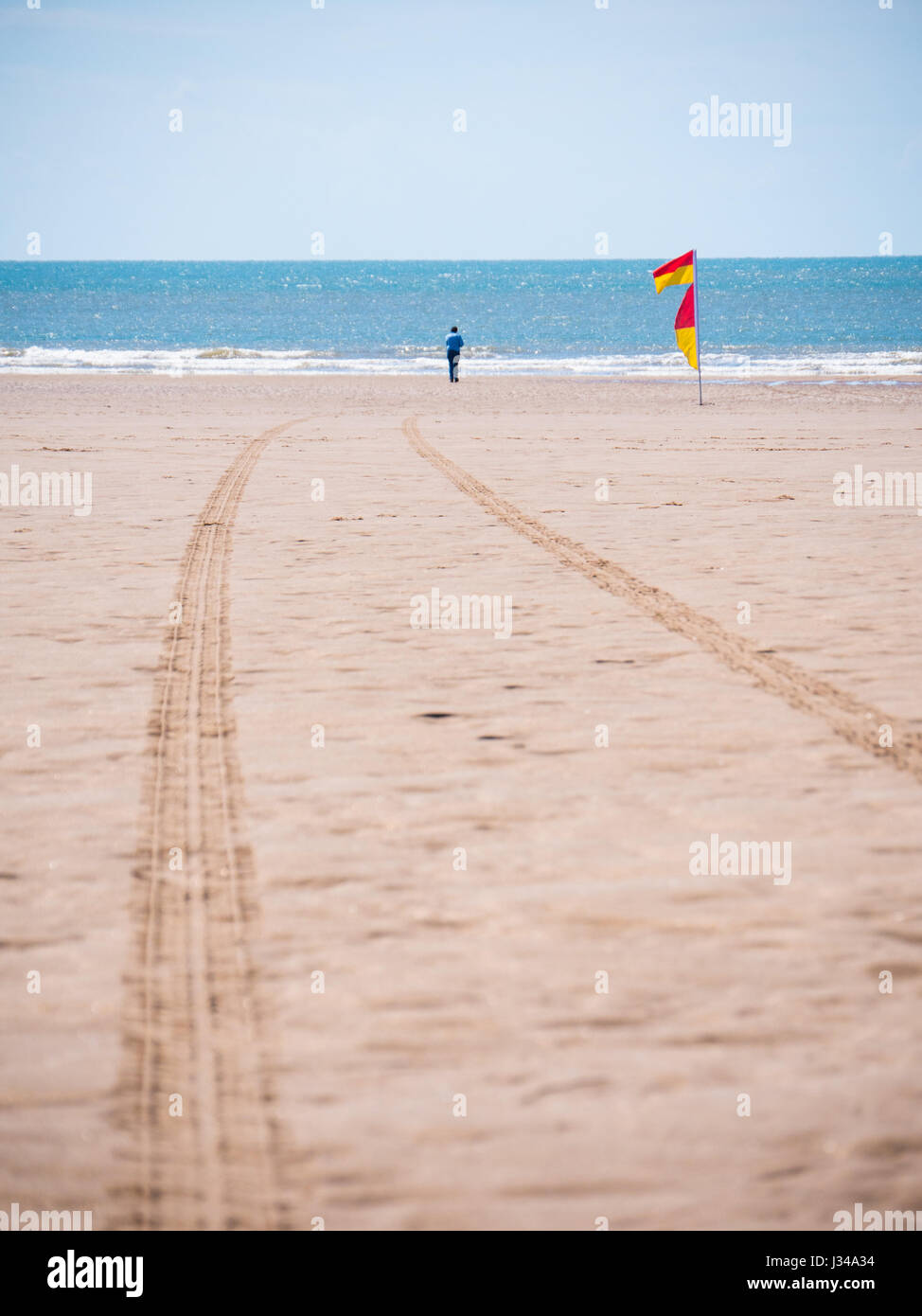 Man walking towards beach flags and the surf at Croyde beach on a ...