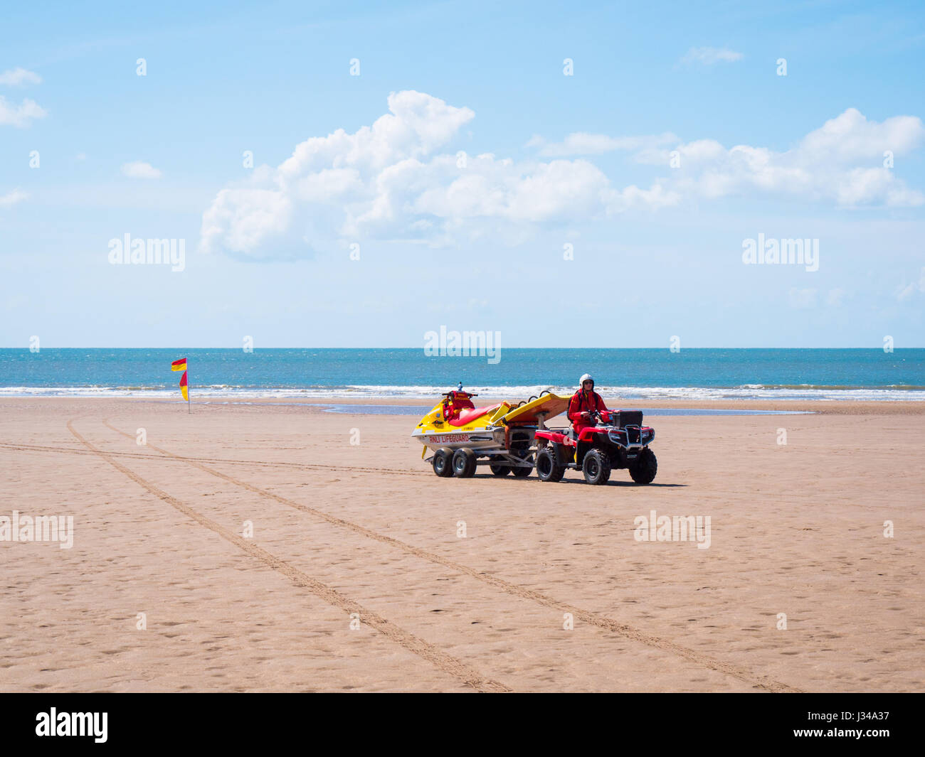 RNLI lifeguard quadbike towing jet ski drives along the beach at Croyde ...