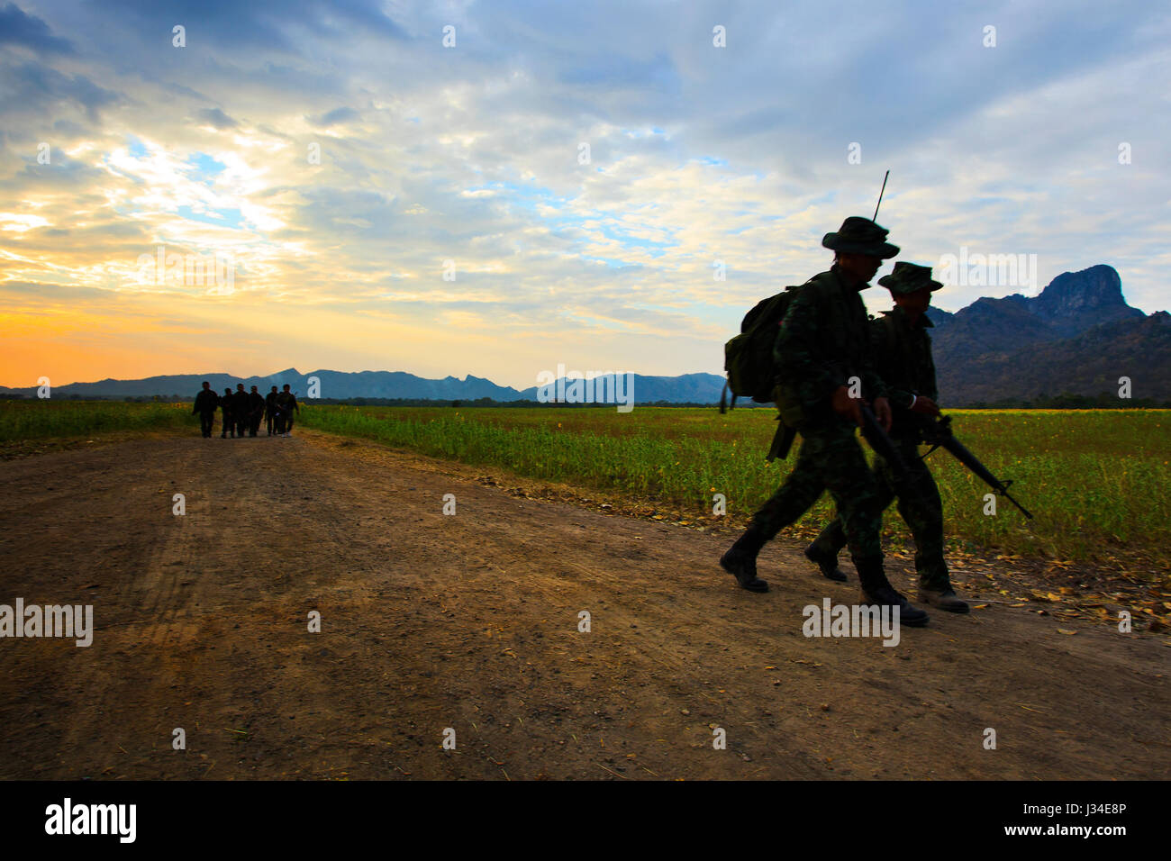 silhouette motion of long range patrolling soldier walking on dirt road ...