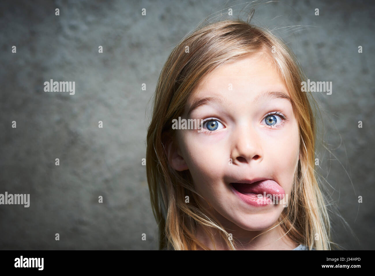 little child blond girl making faces with gray grunge wall background ...