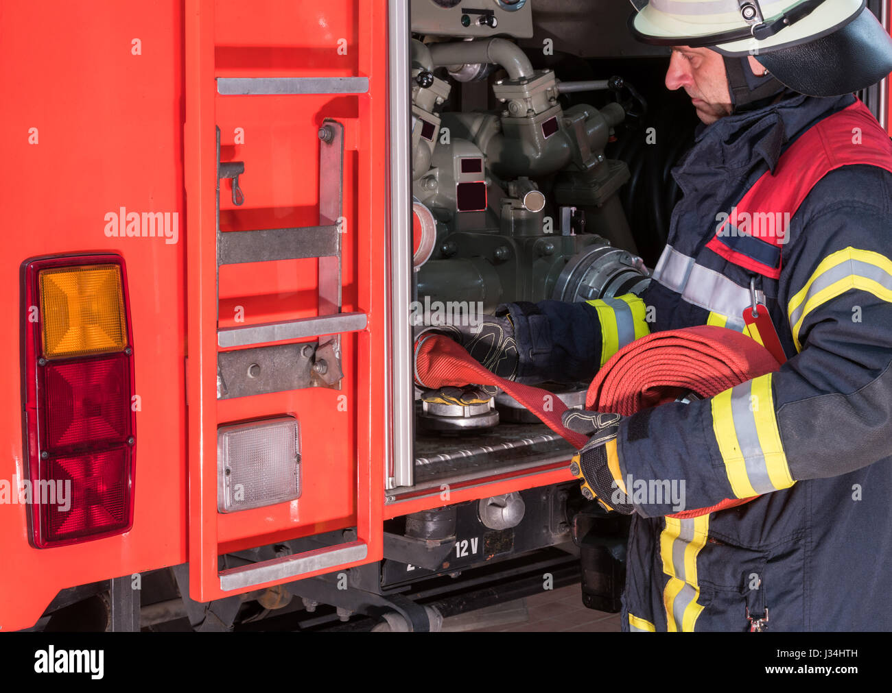 German firefighter wearing a rolled fire hose to the fire truck Stock ...