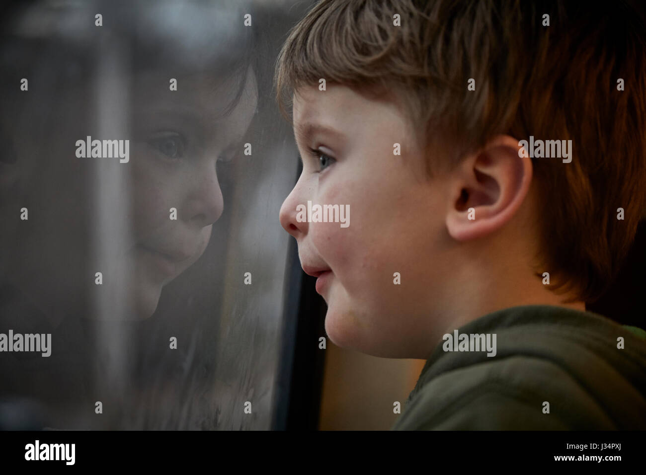 Boy on a train staring out of the window with his face reflecting in ...