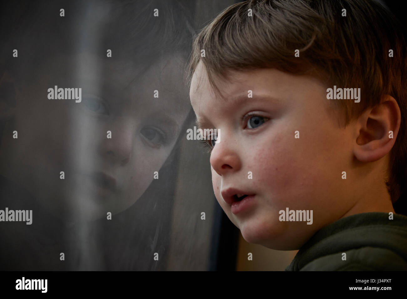 Boy on a train staring out of the window with his face reflecting in ...