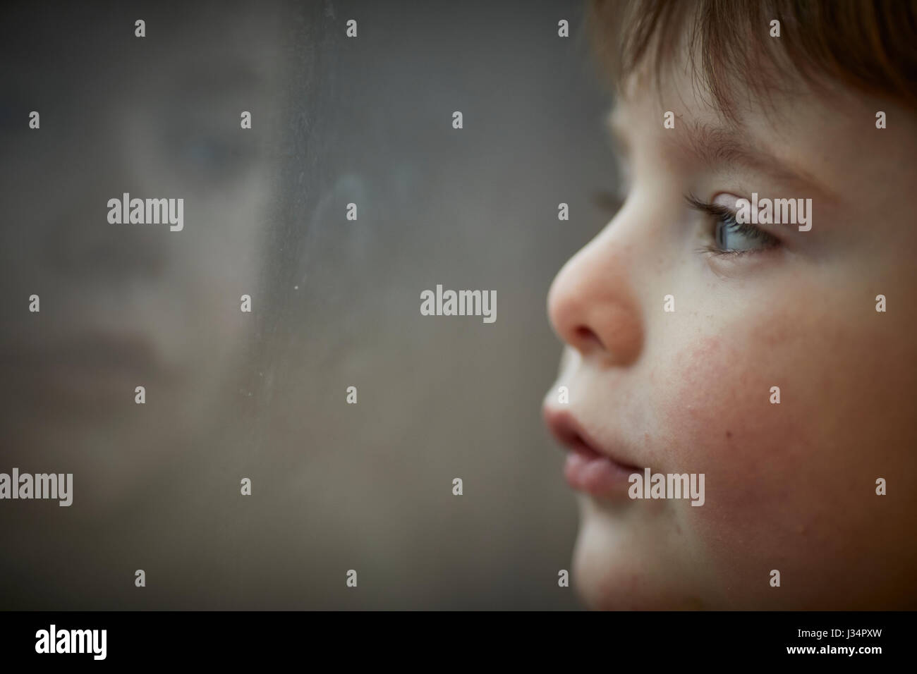Boy on a train staring out of the window with his face reflecting in ...