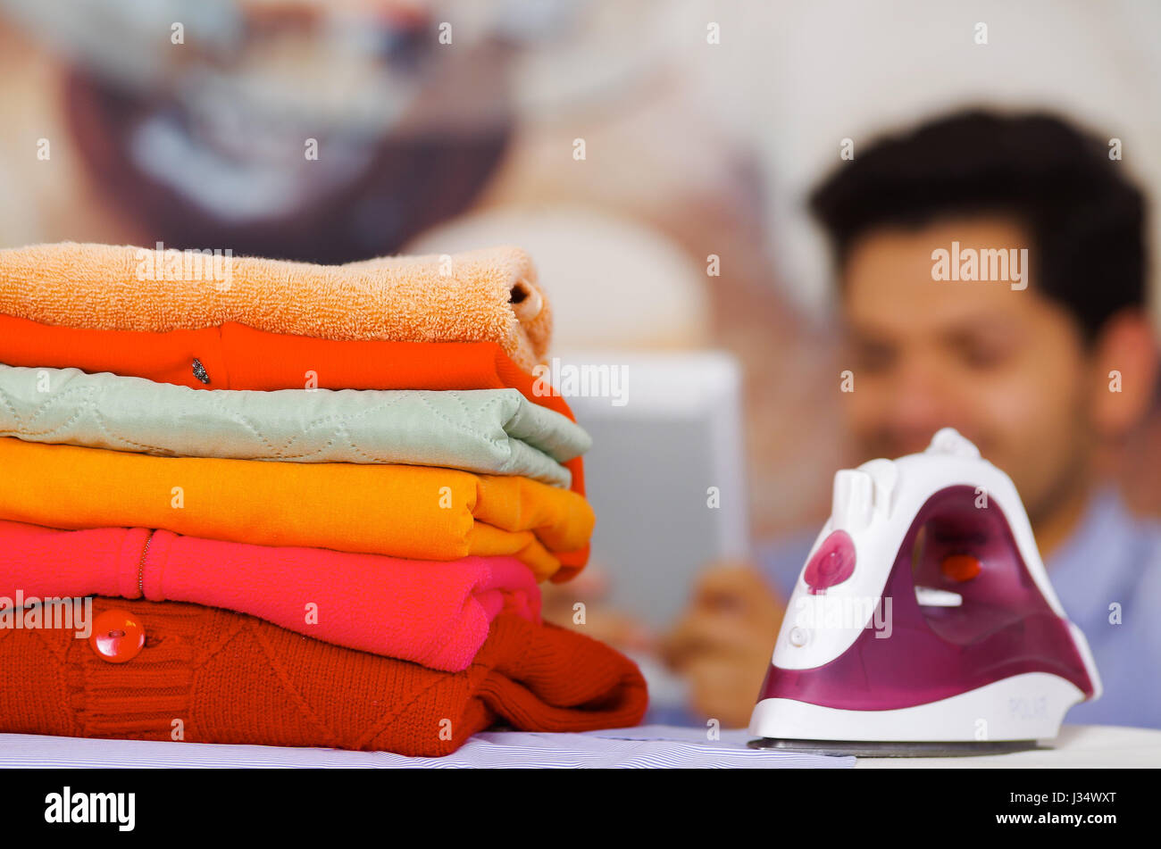 A pile of clothes next to the iron with gorgeous man smiling behind ...