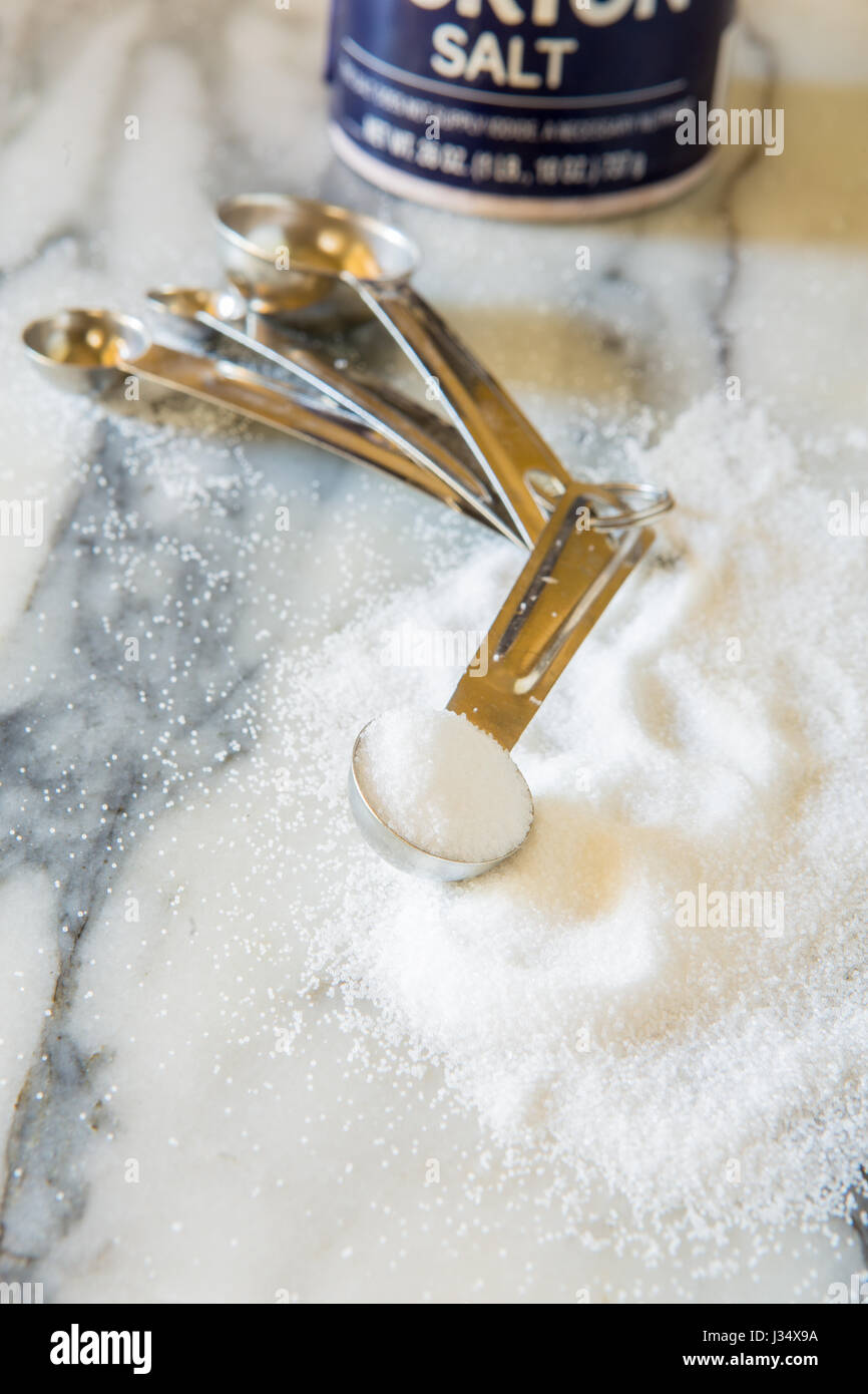 A teaspoon of salt being measured on a marble counter top in a home ...