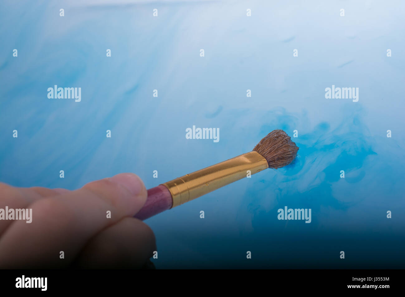 Watercolor paint dissolving in water as painting brush touches water ...