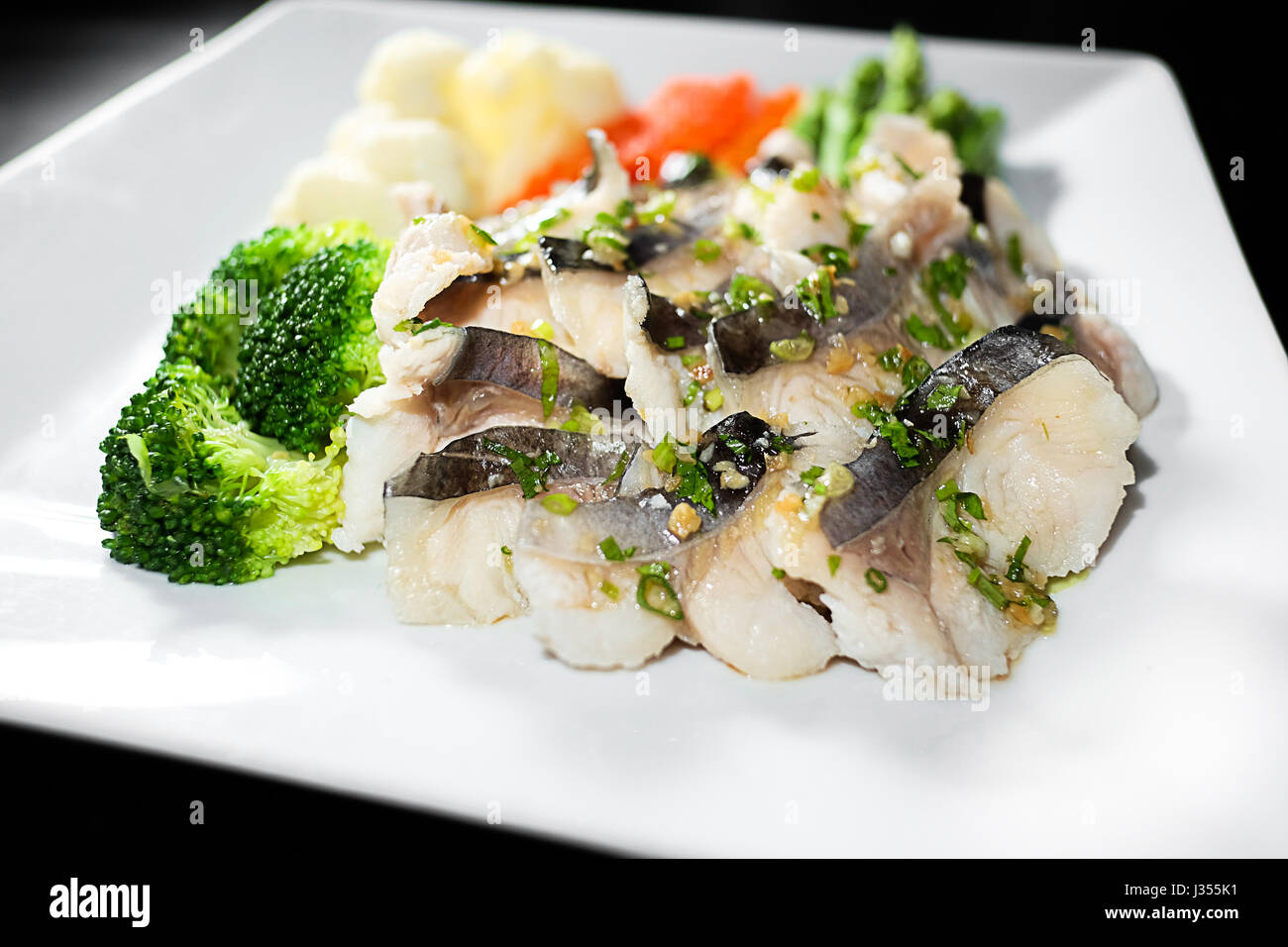 Slice steamed fish with braised leeks topping and spicy sauce in black ...