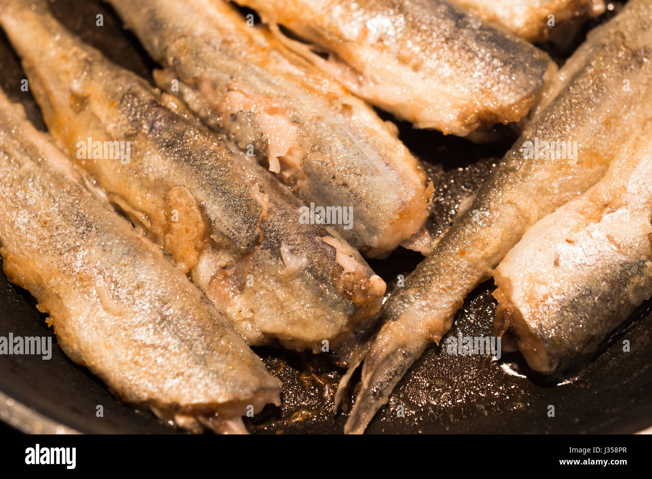 Small golden wild fish packed in rows, fried in a pan, covered with a ...