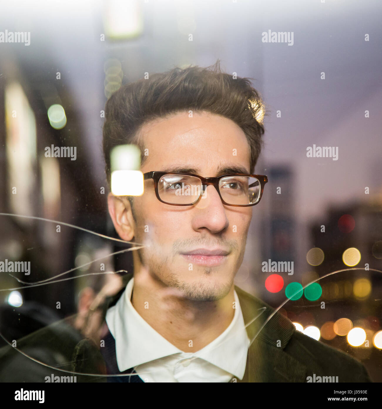 Portrait of a young handsome man with short hair posing behind a glass ...