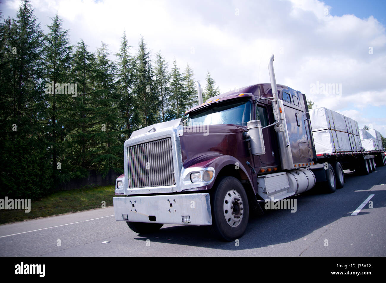Powerful bonneted semi truck transports packed stacks of lumber boards ...