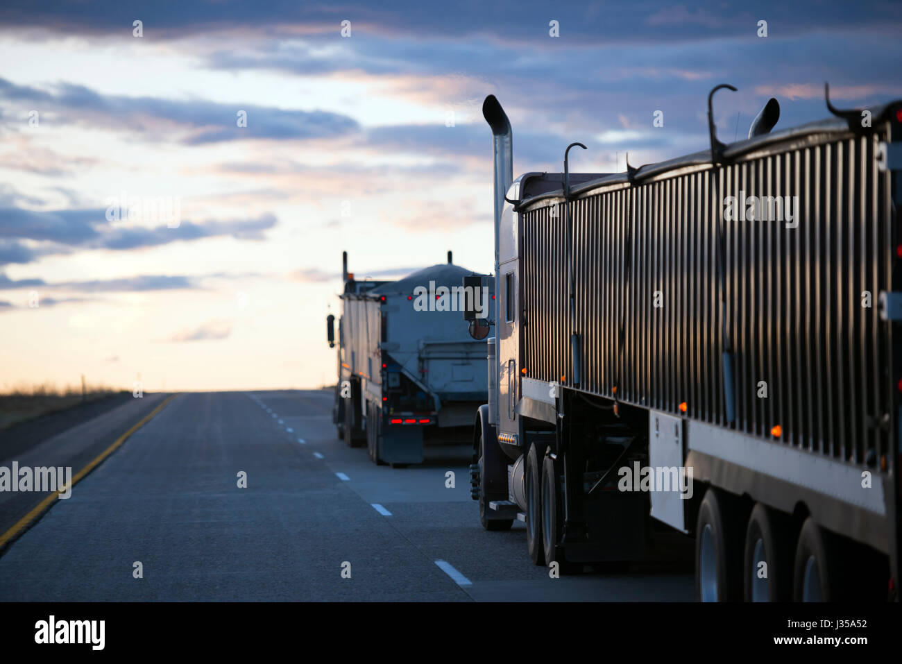 Several semi trucks with bulk cargo trailers move by convoy on the road ...