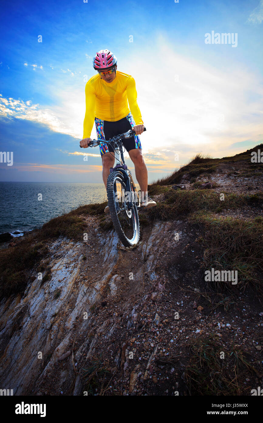 young man riding moutain bike mtb on land dune against dusky sky in ...