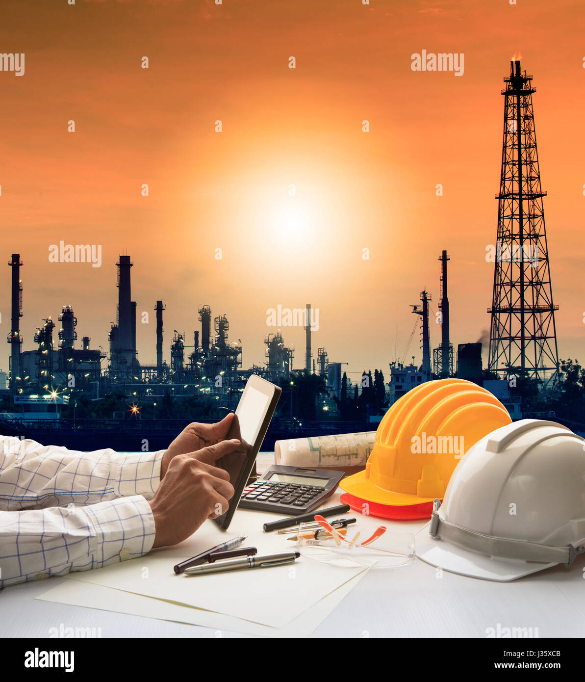 engineering working on computer tablet against silhouette of oil ...