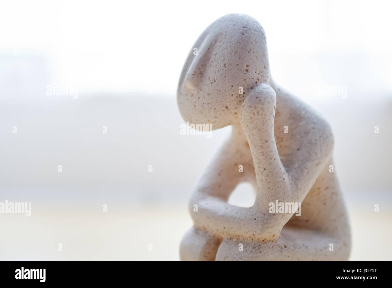 small statue of stone man thinking, pause for thought, light background ...