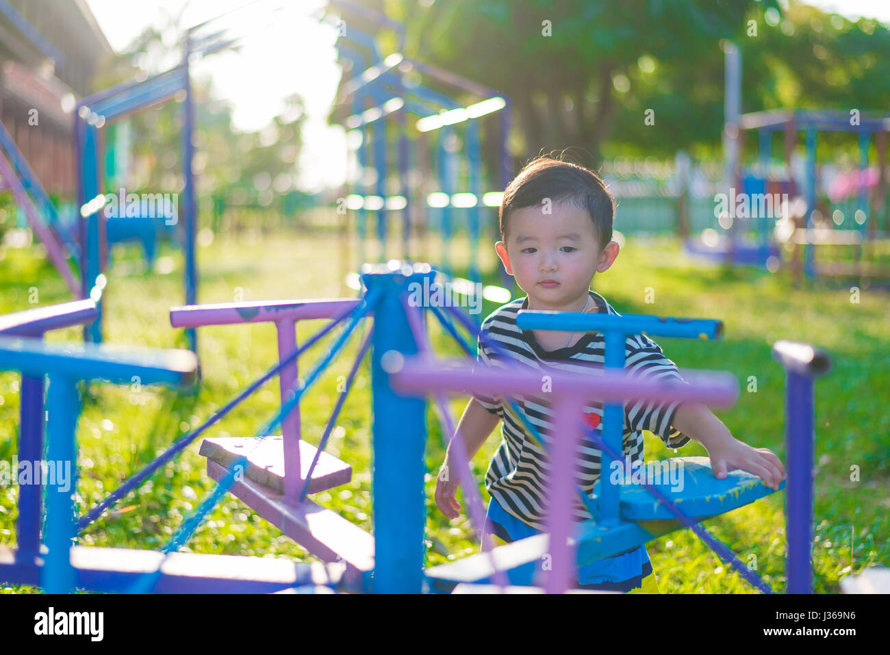 Sad little Asian kid at the playground under the sunlight in summer ...